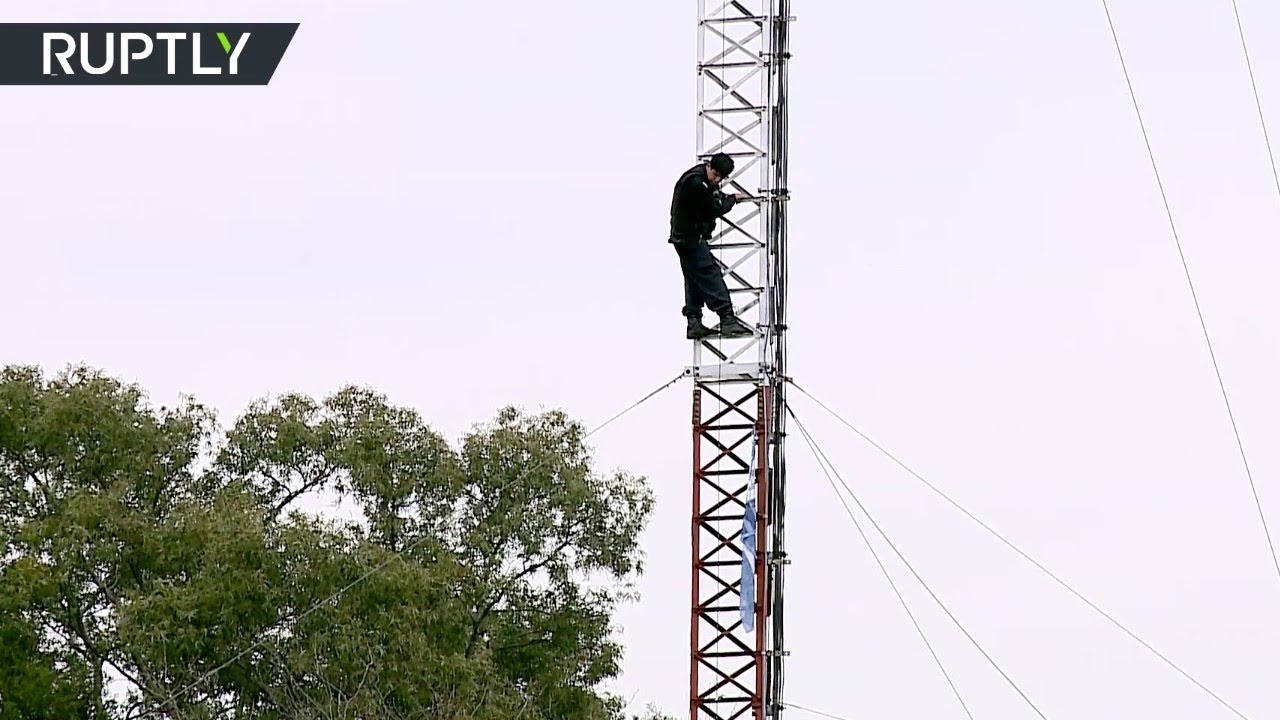 Police officer scales power pylon & threatens to jump during protest in ...