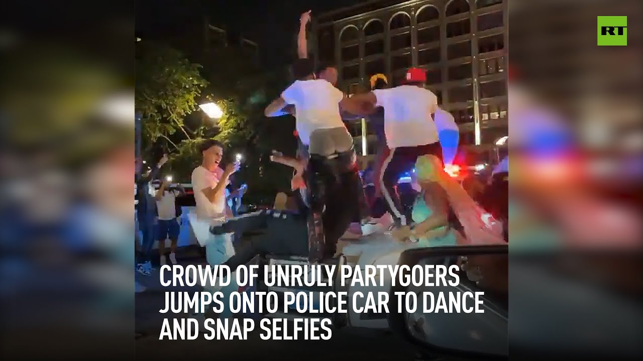 Crowd of unruly party-goers jumps onto police car to dance and snap ...